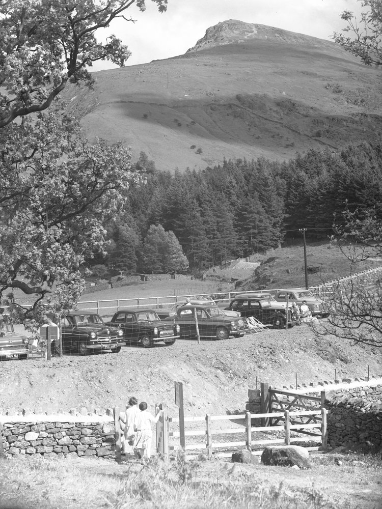 Two girls walking through a gate towards parked cars with hill behind