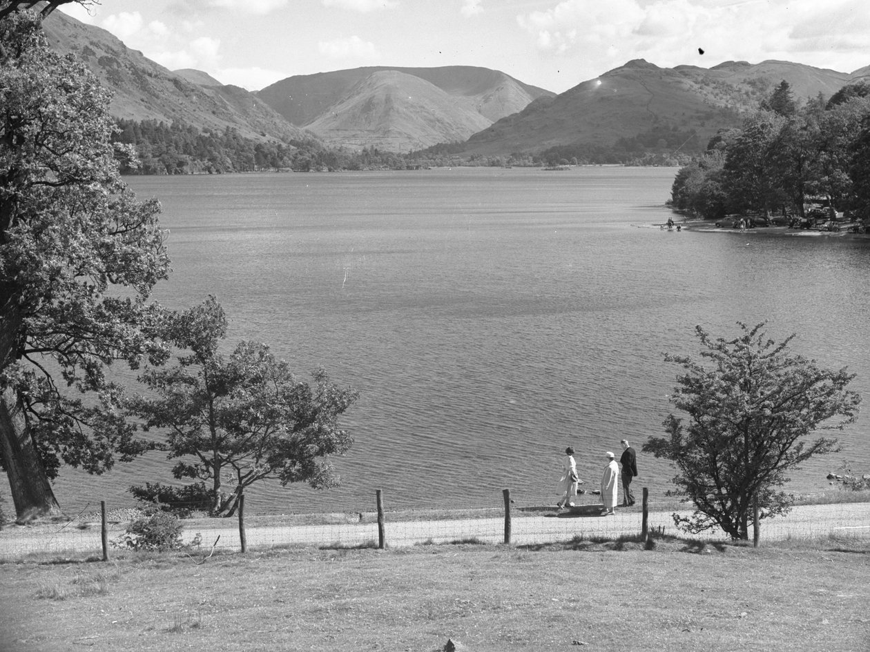 A man, lady and possibly their daughter stroll along the edge of a lake ...